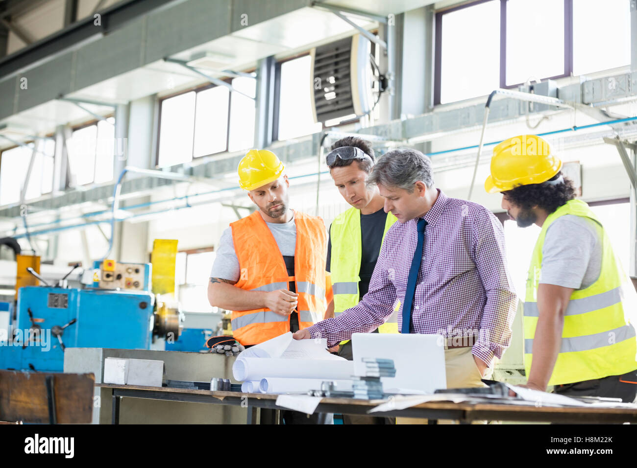 Supervisor with workers examining blueprints at table in industry Stock ...