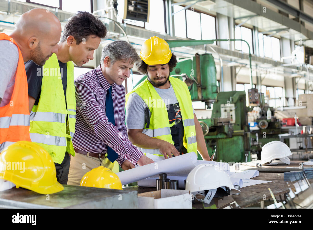 Male supervisor with workers discussing over blueprints in industry ...