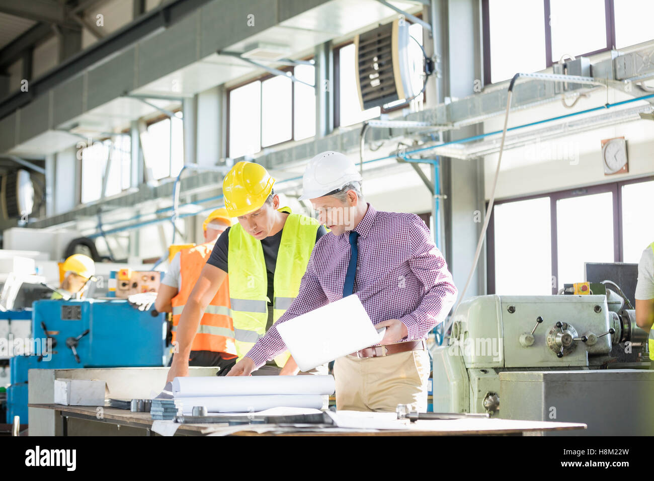 Architect and manual worker examining blueprint at table in industry ...