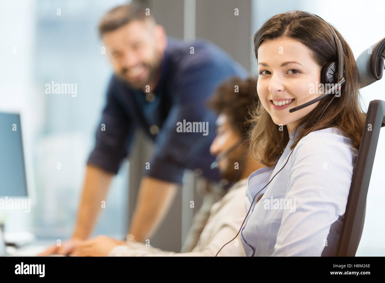 Portrait of young businesswoman wearing headset with colleagues in ...