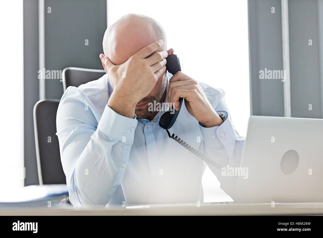 Tired mid adult businessman using landline phone at desk in office ...