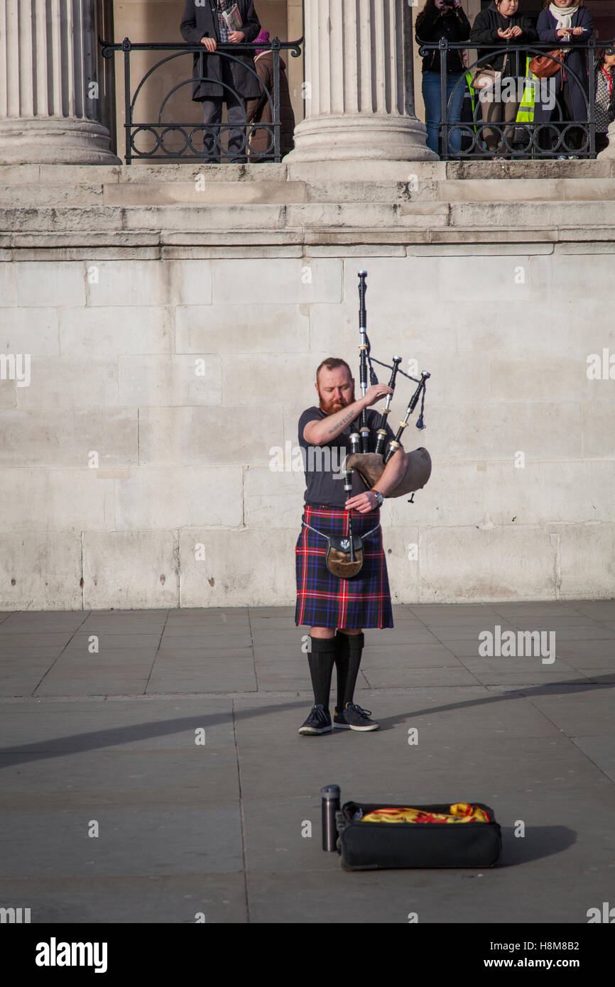 A piper dressed in a tartan kilt, plays his bagpipes for the tourists ...