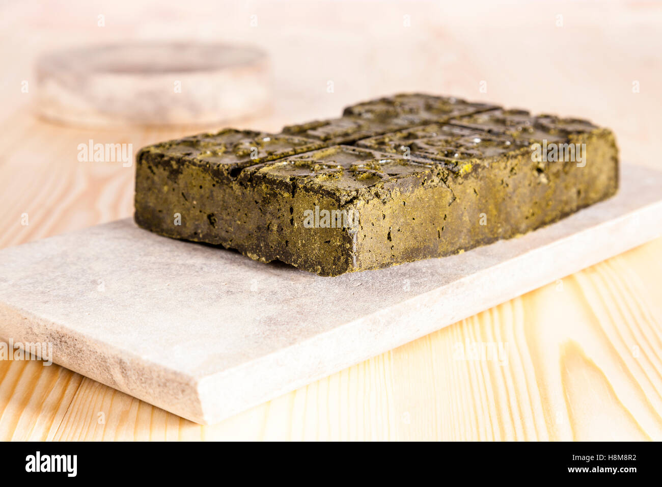 A block of henna on a stone platter placed on a pine wooden surface ...