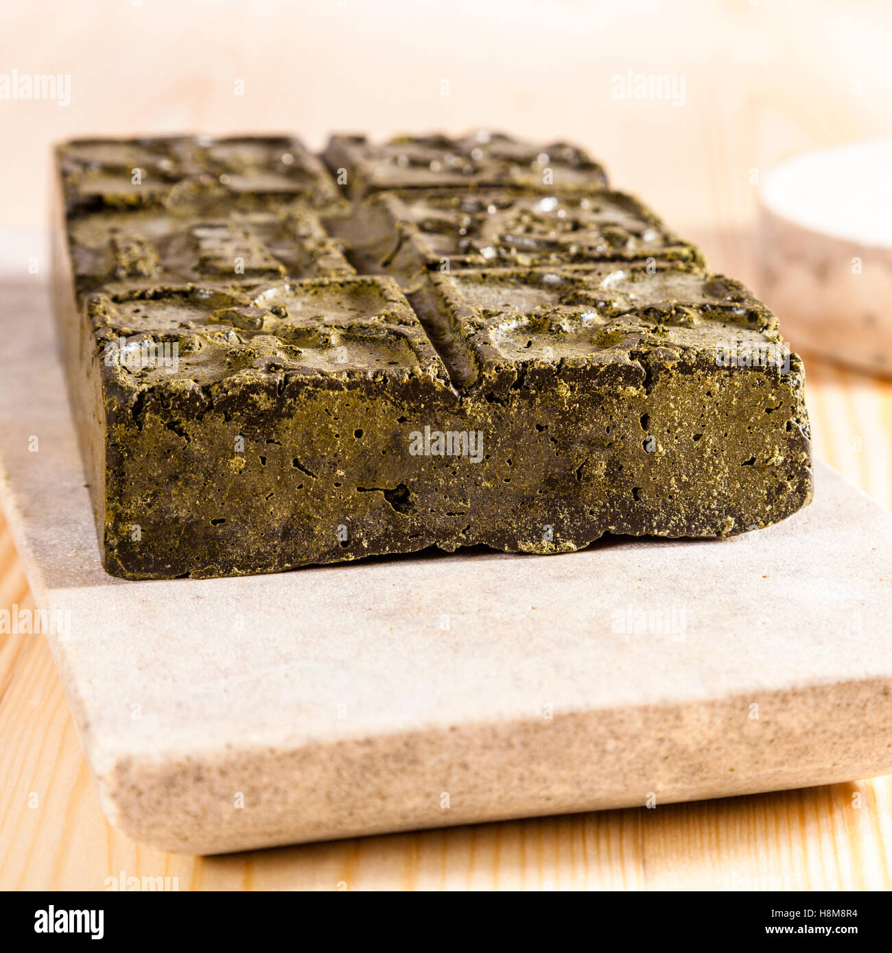 A block of henna on a stone platter placed on a pine wooden surface ...