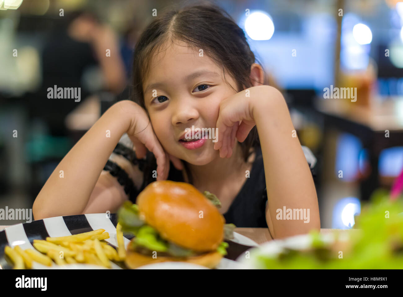 Hungry Asian child eating hamburger at restaurant Stock Photo - Alamy
