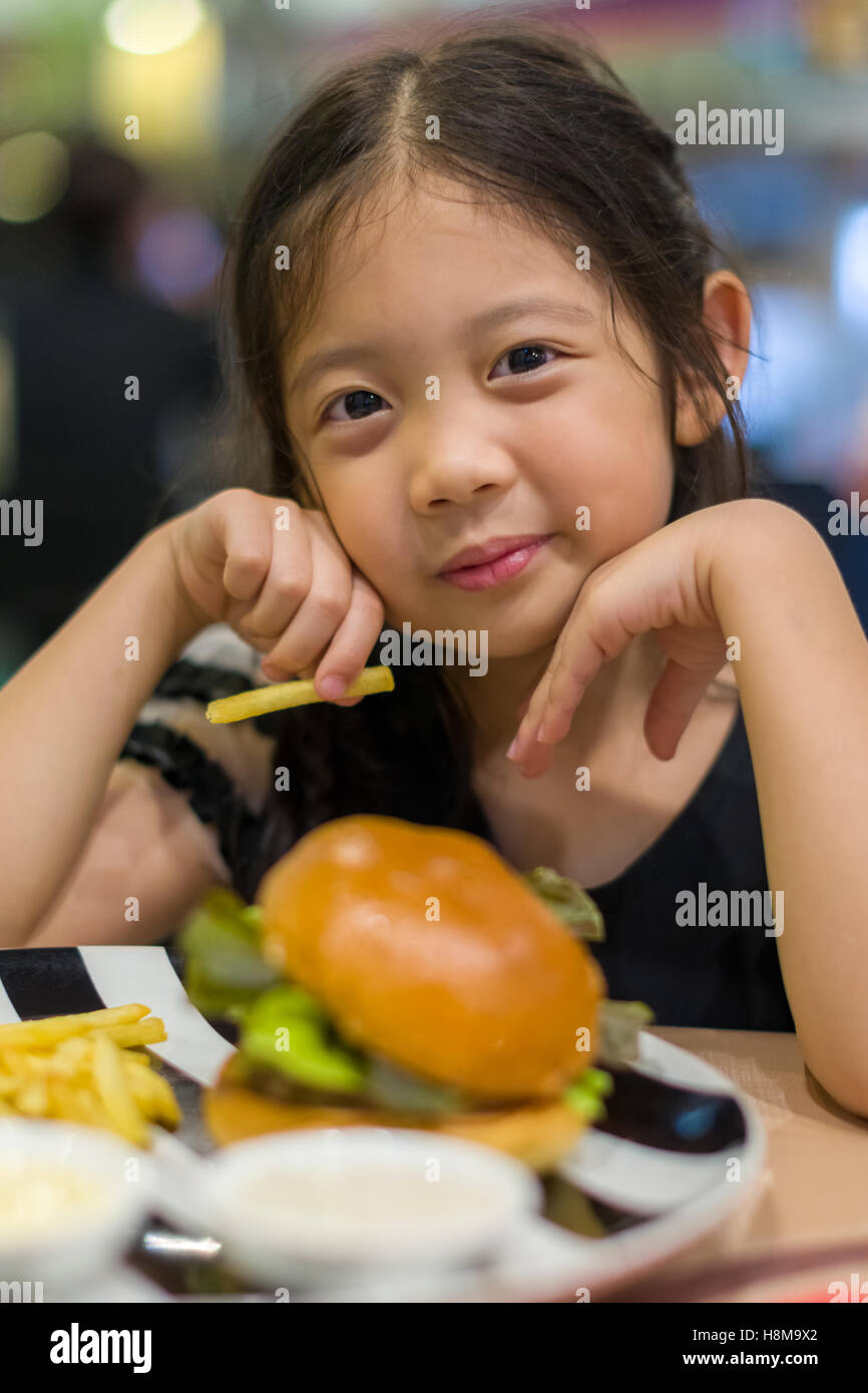 Hungry Asian kid eating hamburger at restaurant Stock Photo - Alamy