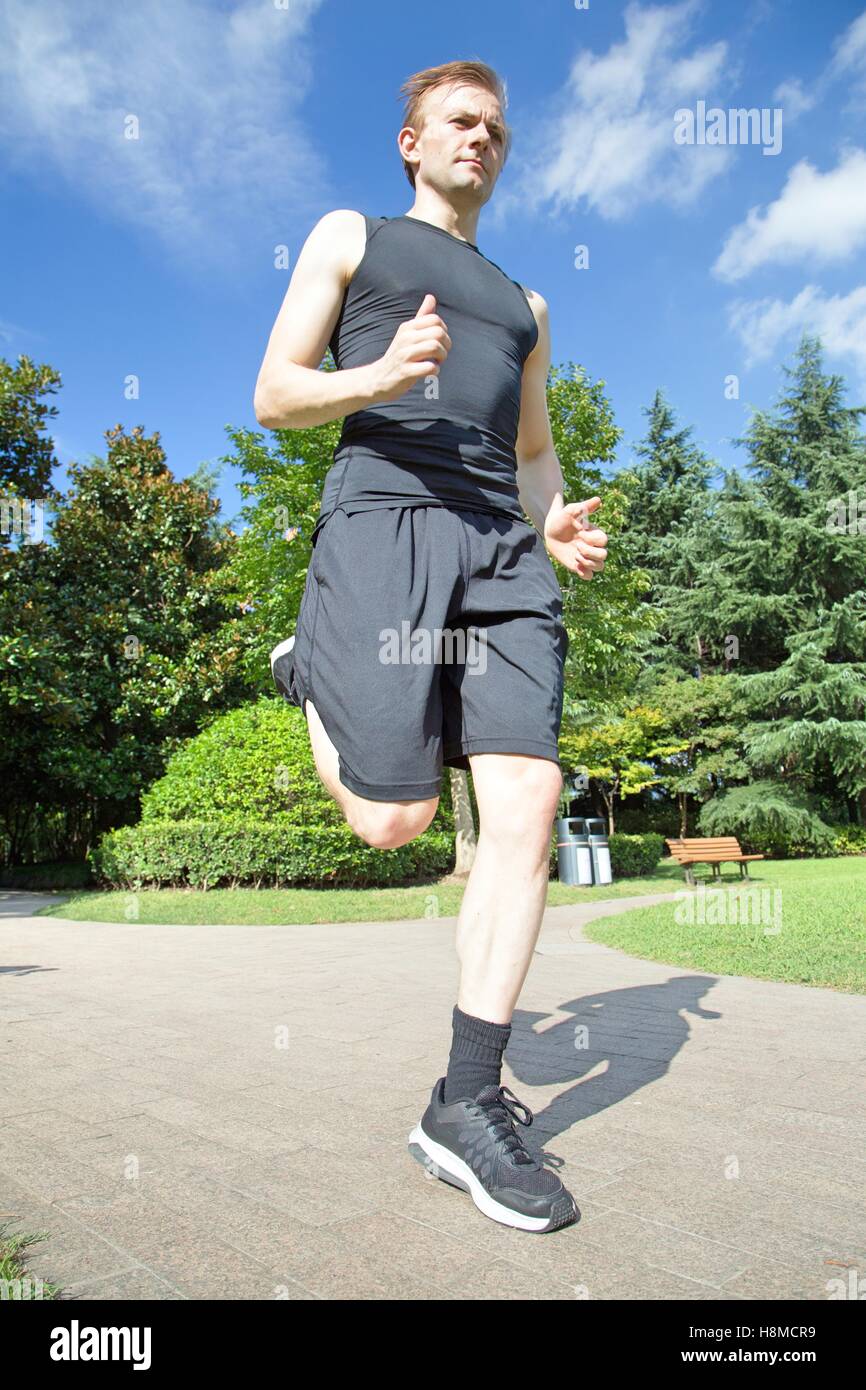 Low angle front view of caucasian man running in park Stock Photo - Alamy