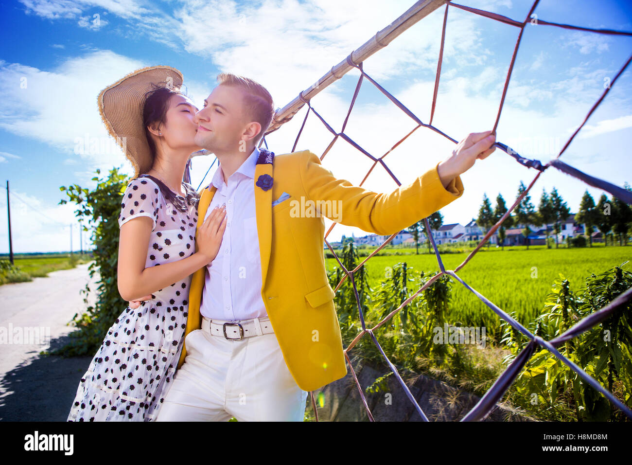 Woman kissing man while standing by fence at field against sky Stock ...