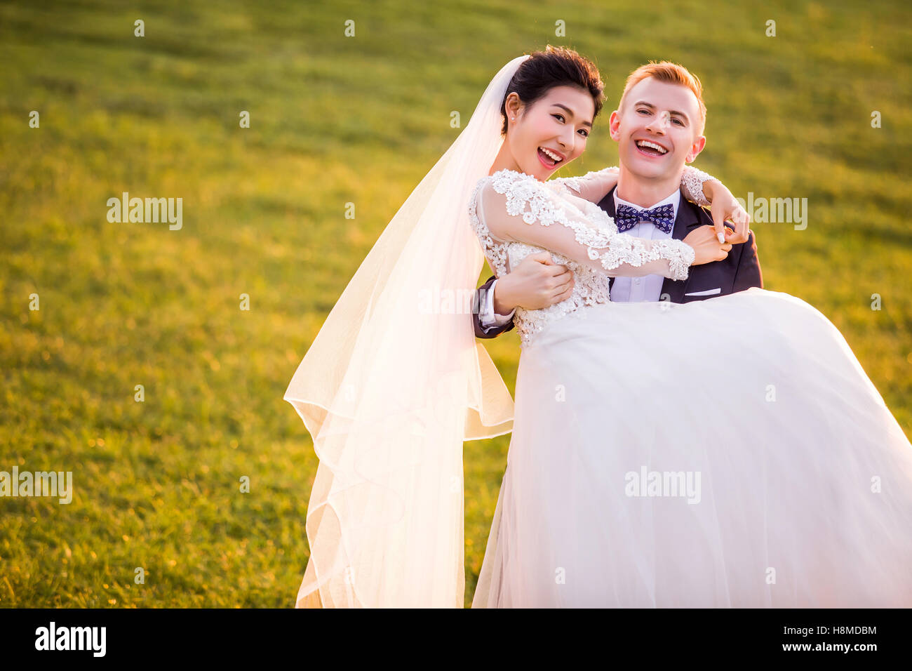 Portrait of cheerful bridegroom carrying bride on grassy field Stock ...