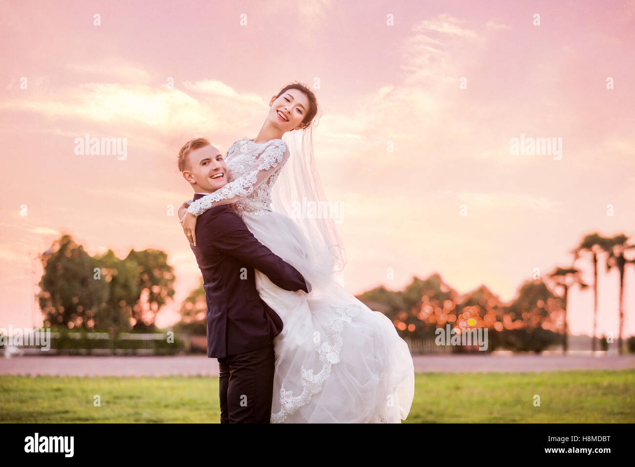 Side view portrait of happy bridegroom carrying bride on field during ...