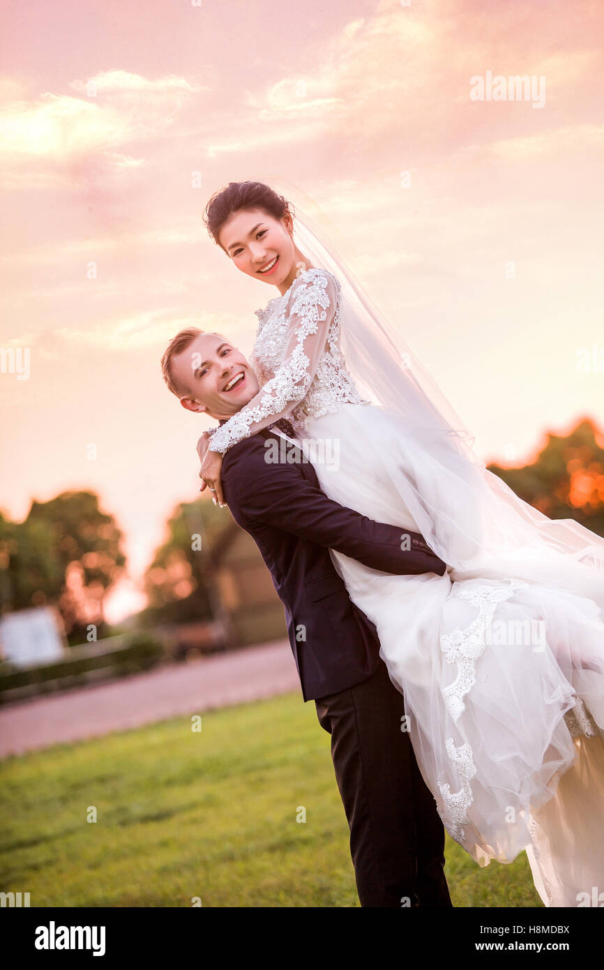 Portrait of happy bridegroom carrying bride on field during sunset ...