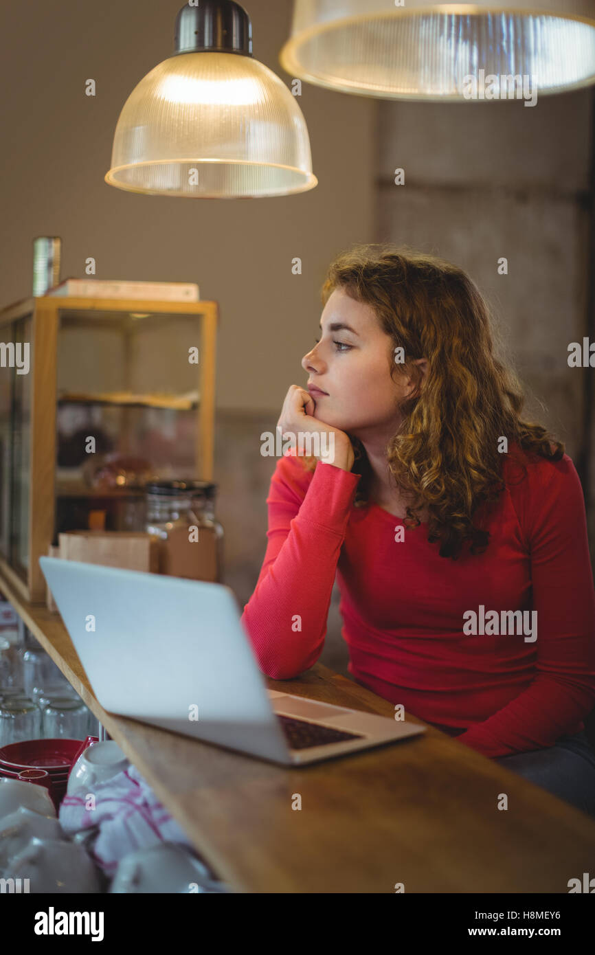 Thoughtful woman sitting at counter with laptop Stock Photo - Alamy