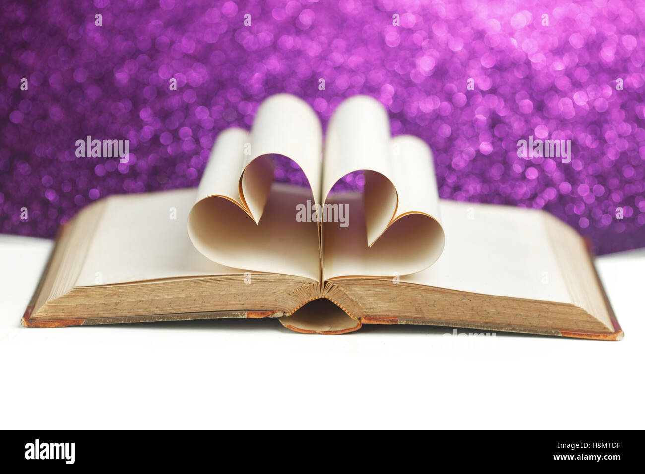 Pages of open book rolled in heart shape on glitter background Stock ...