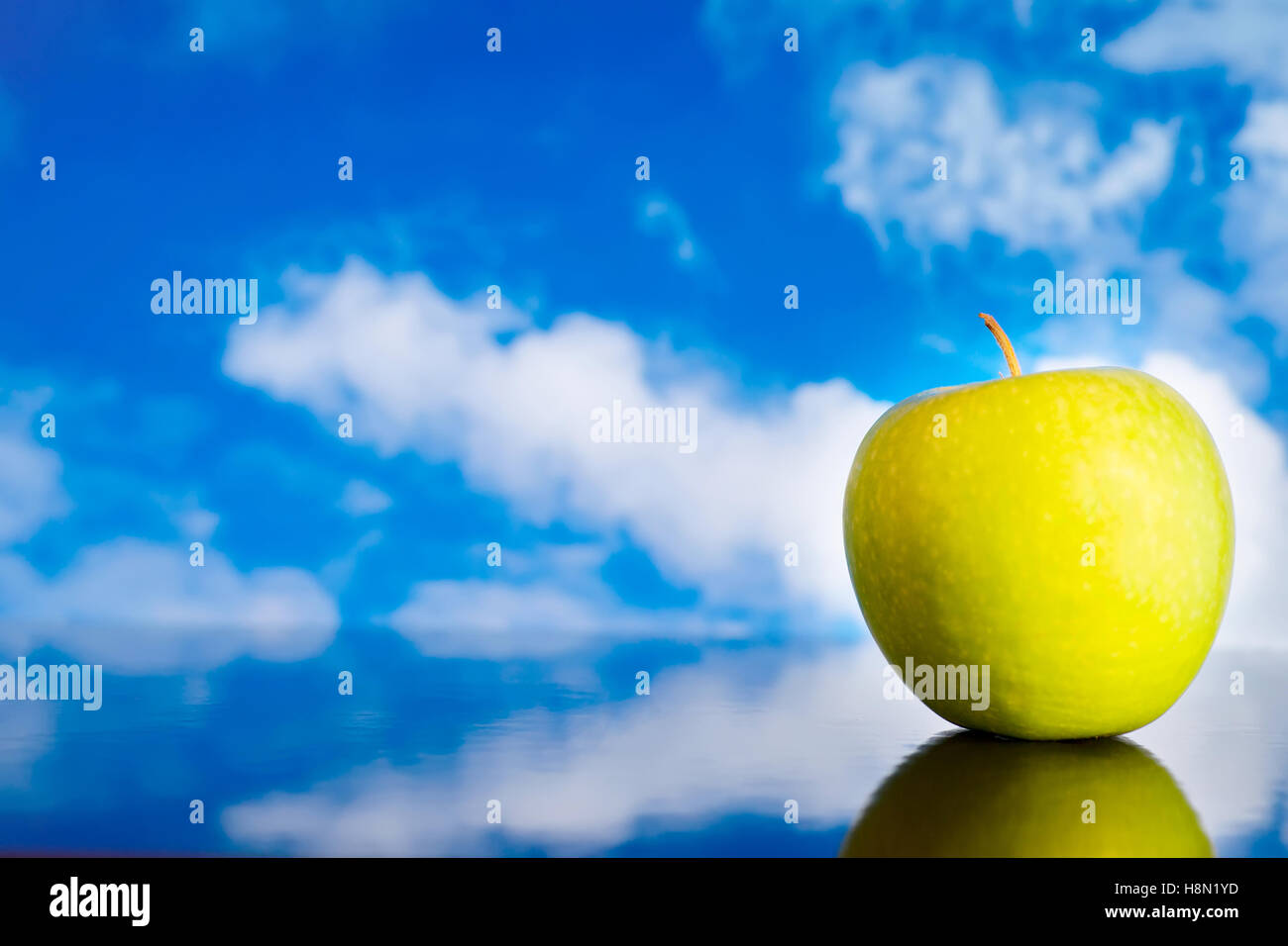 Green apple against blue sky. Display table with reflection for ...