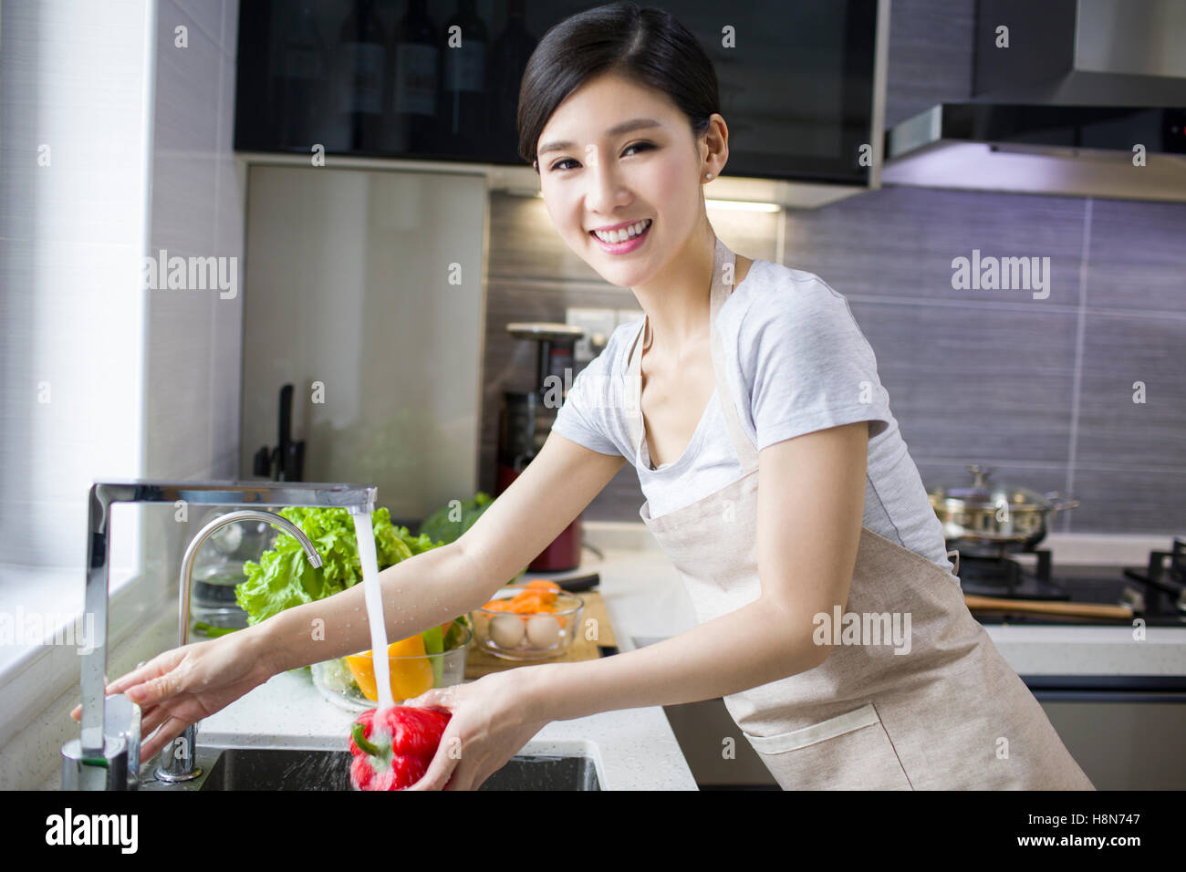 Happy young Chinese woman washing vegetables in kitchen Stock Photo - Alamy