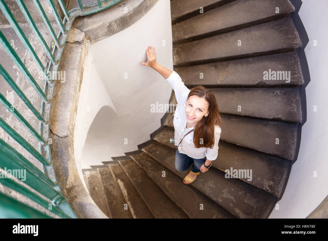 Young smiling woman looking upward and stepping down at curved stairs ...