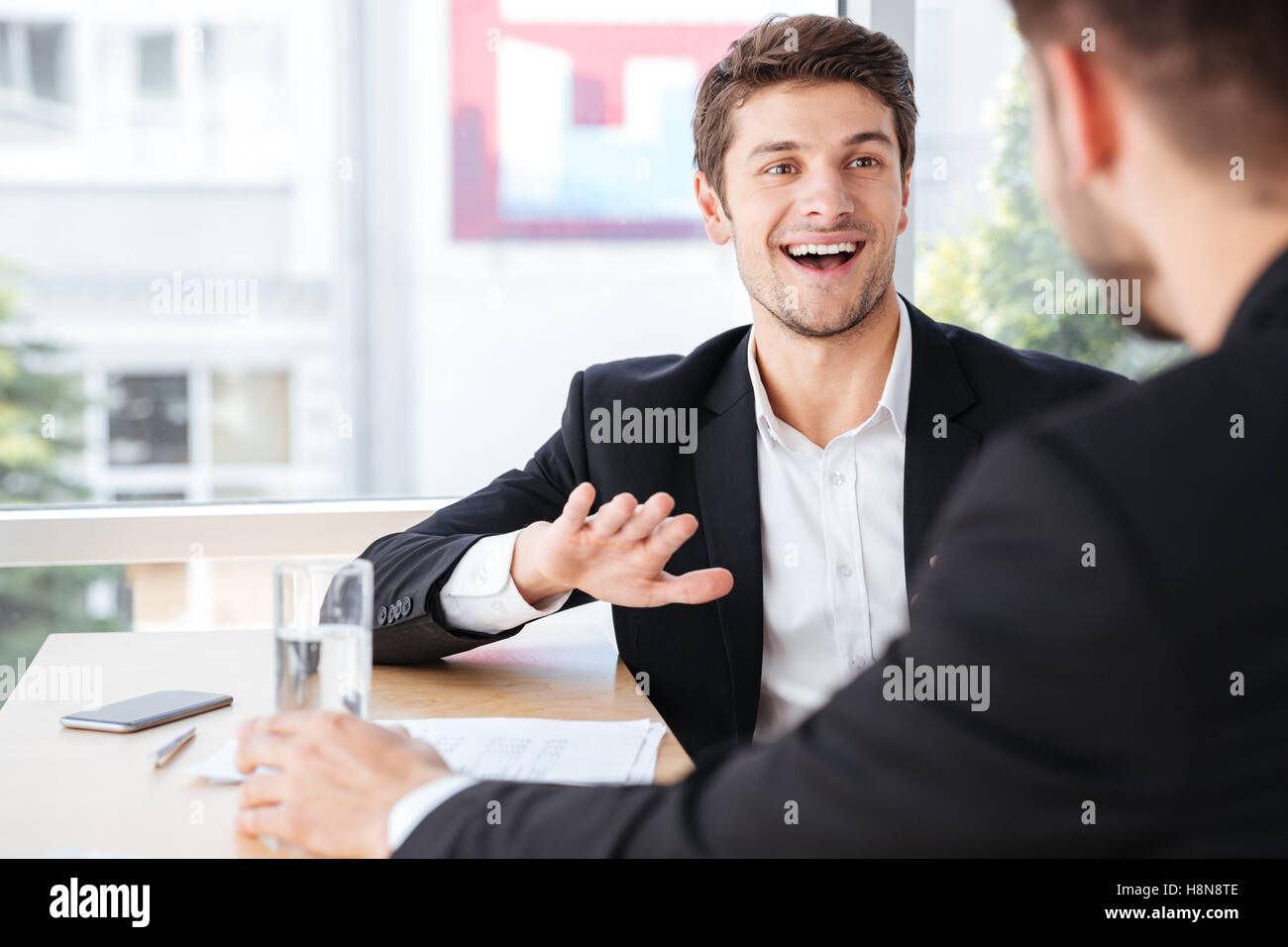 Cheerful young businessman talking with his colleague on business ...