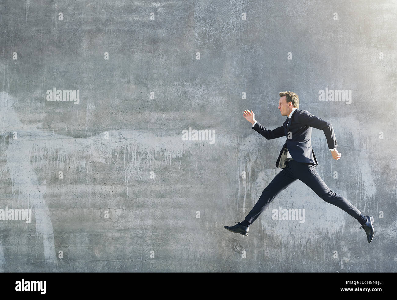 Side view of man in suit caught in jump making pose of walking on grey ...