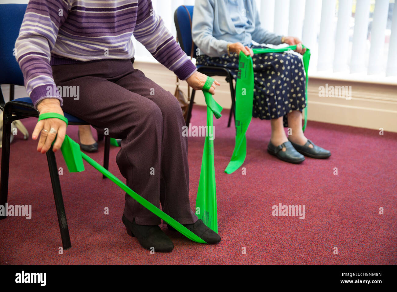 Elderly person in sitting down exercise class using resistance band ...
