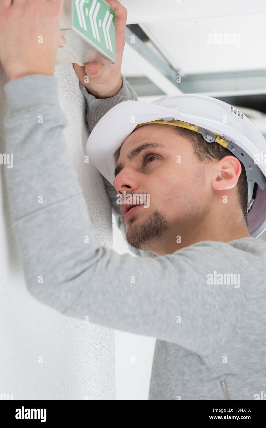 Man fixing fire evacuation sign to wall Stock Photo - Alamy