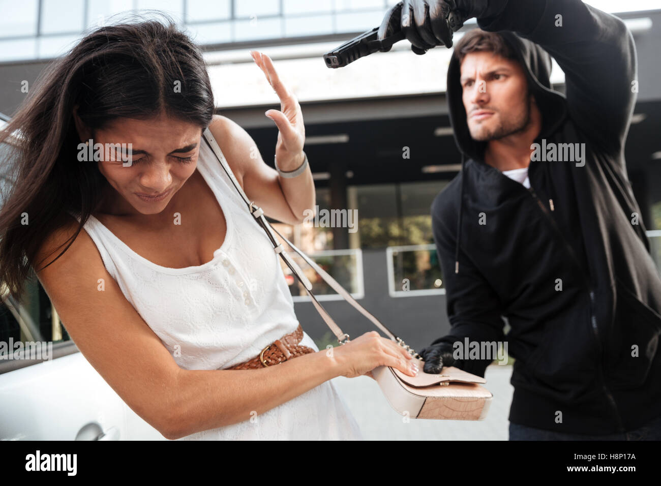 Aggressive young man with gun trying to steal purse of frightened young ...