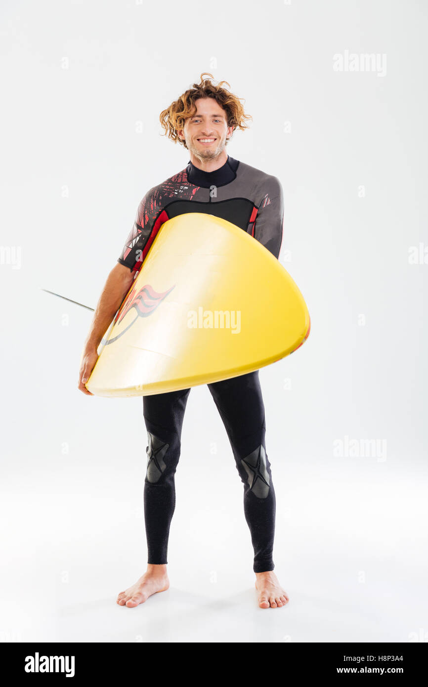 Full length portrait of a young smiling surfer holding surf board ...