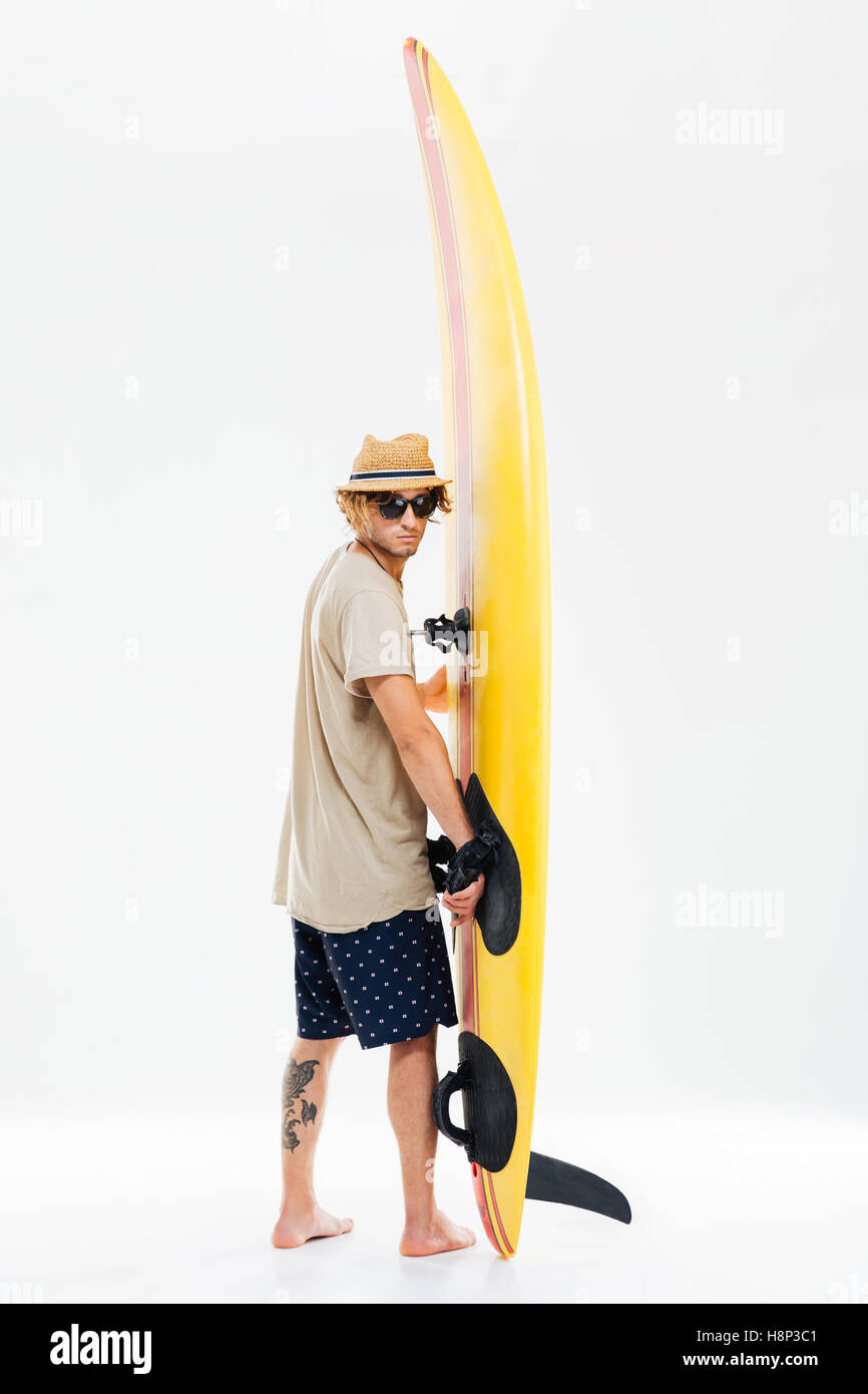 Back view a young surfer holding surfboard and looking over his ...