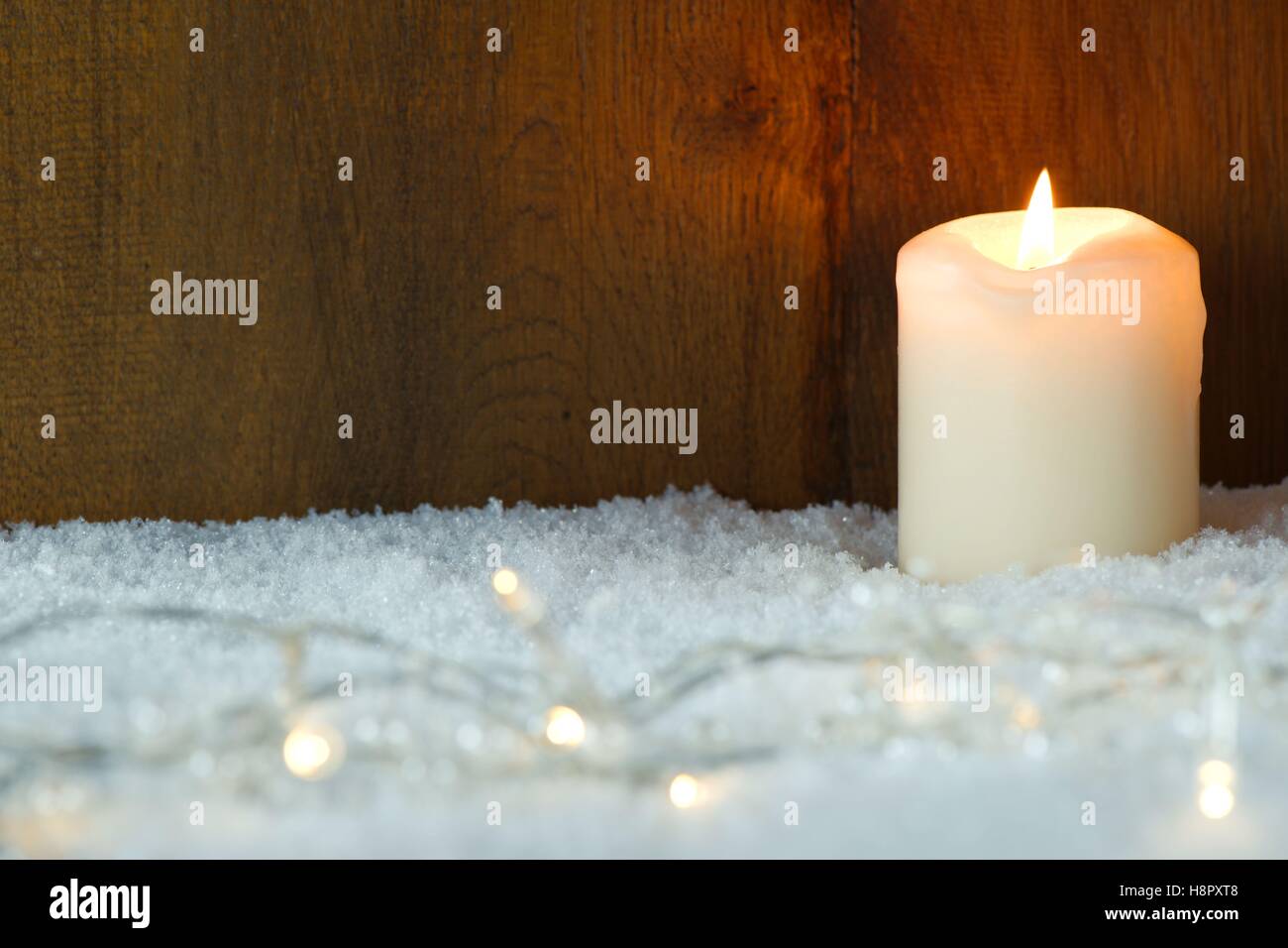 Burning candle with Christmas lights in snow Stock Photo - Alamy