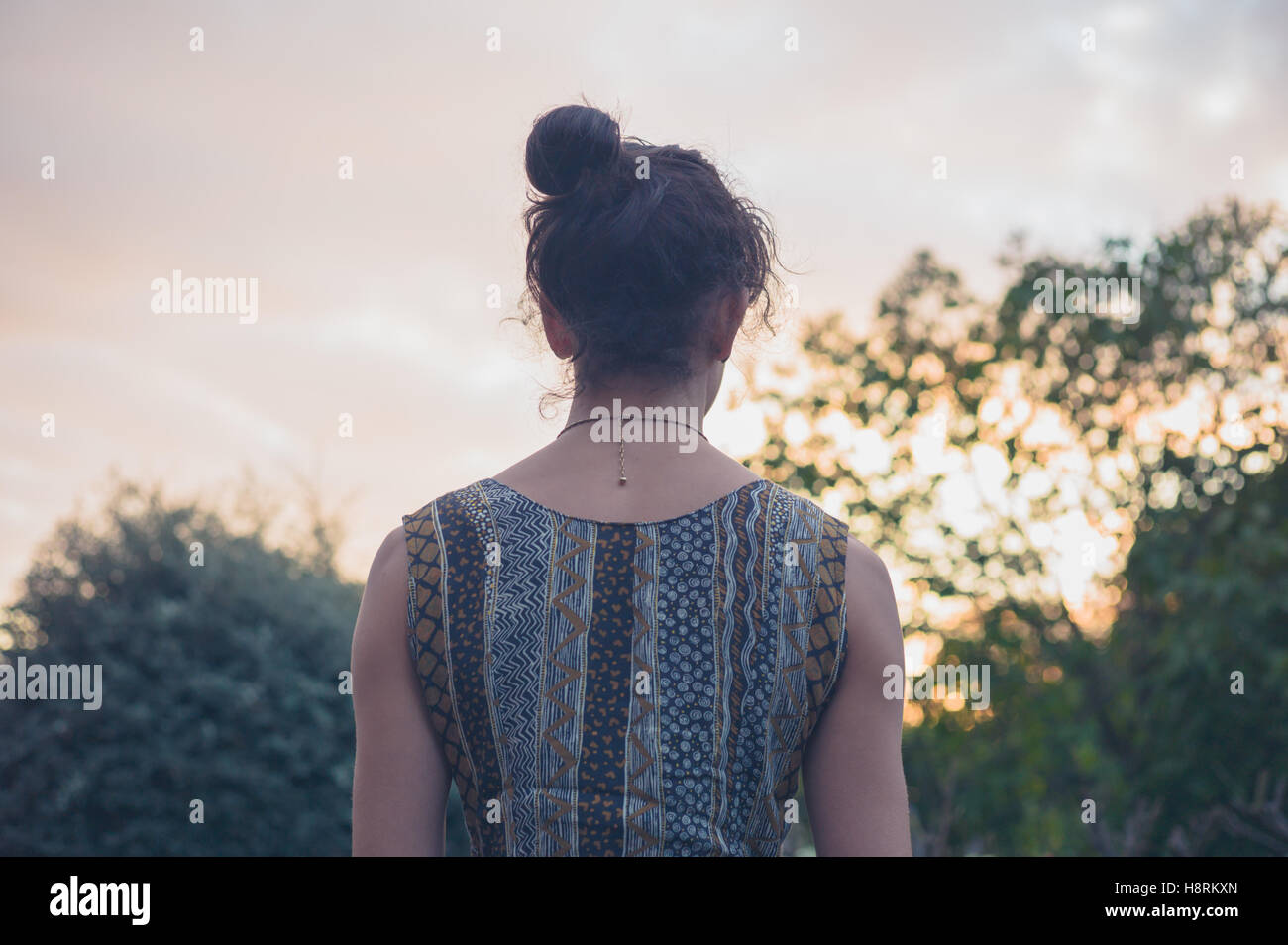 Rear view shot of a young woman standing outside by some trees at ...
