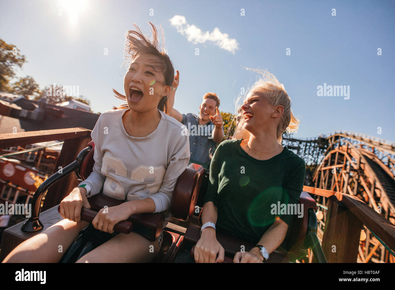 Young friends on thrilling roller coaster ride. Young women and men ...