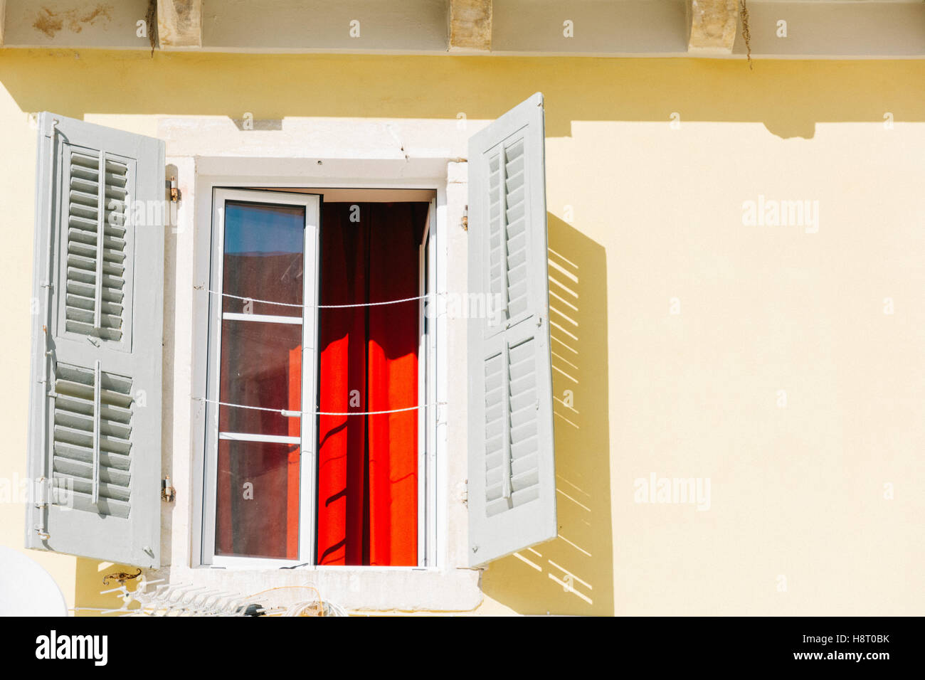 An open window with wooden shutters and red curtains on a sunny day ...