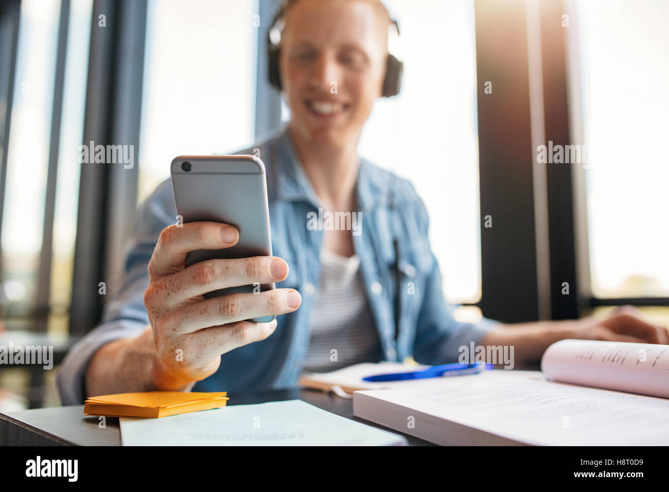Shot of young man reading text message on his mobile phone in a library ...