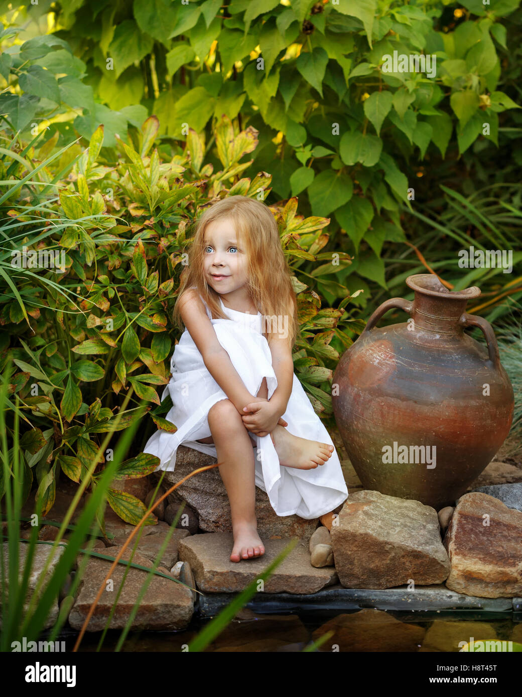 Cute little girl in white dress sitting by the pond with lilies. Old ...