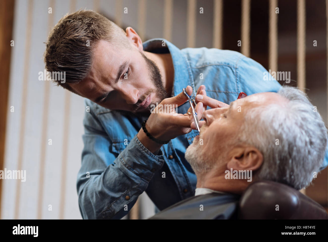 Handsome young barber cutting mustache of senior client with scissors ...