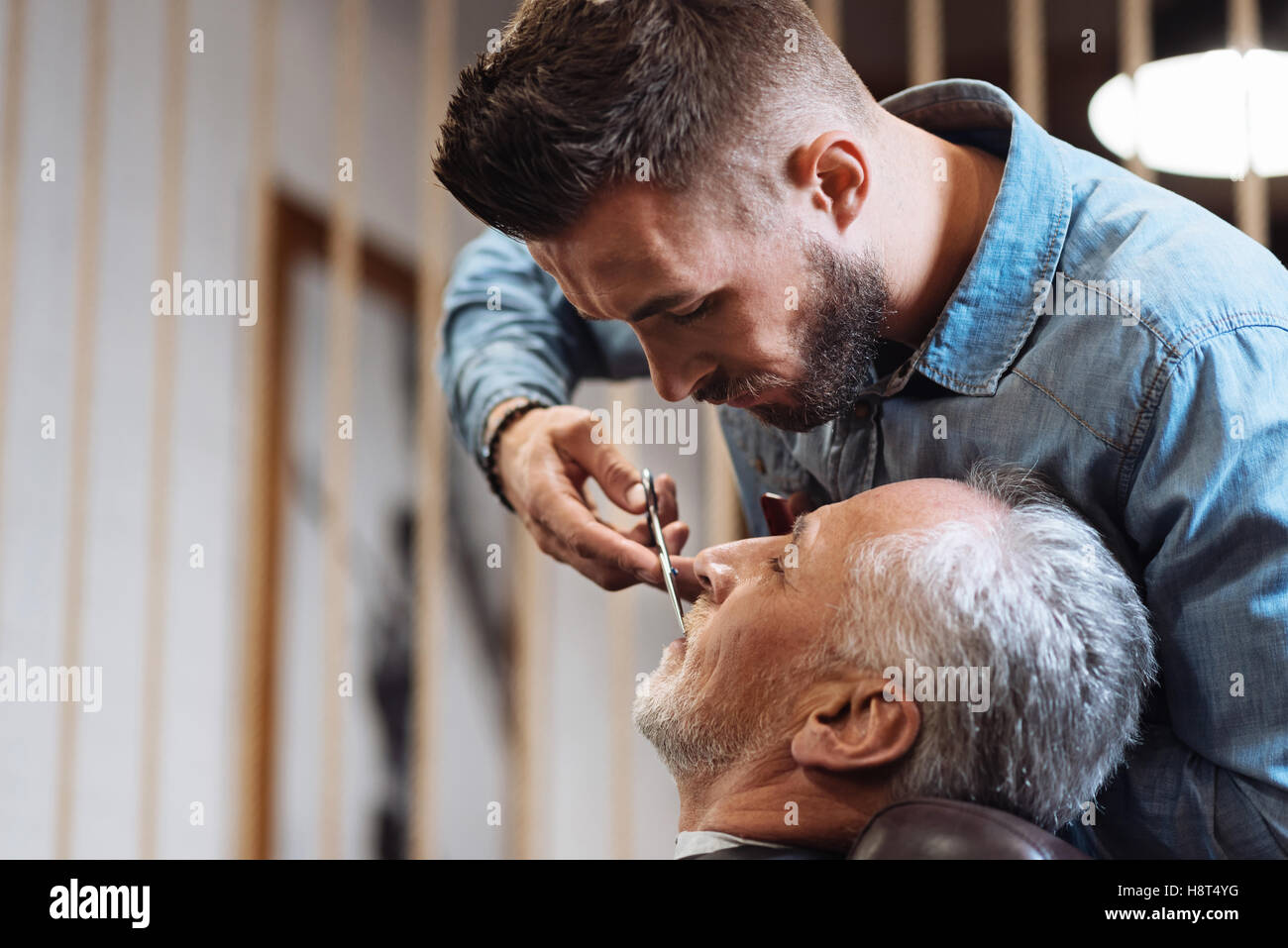 Handsome young barber cutting mustache of senior client with scissors ...