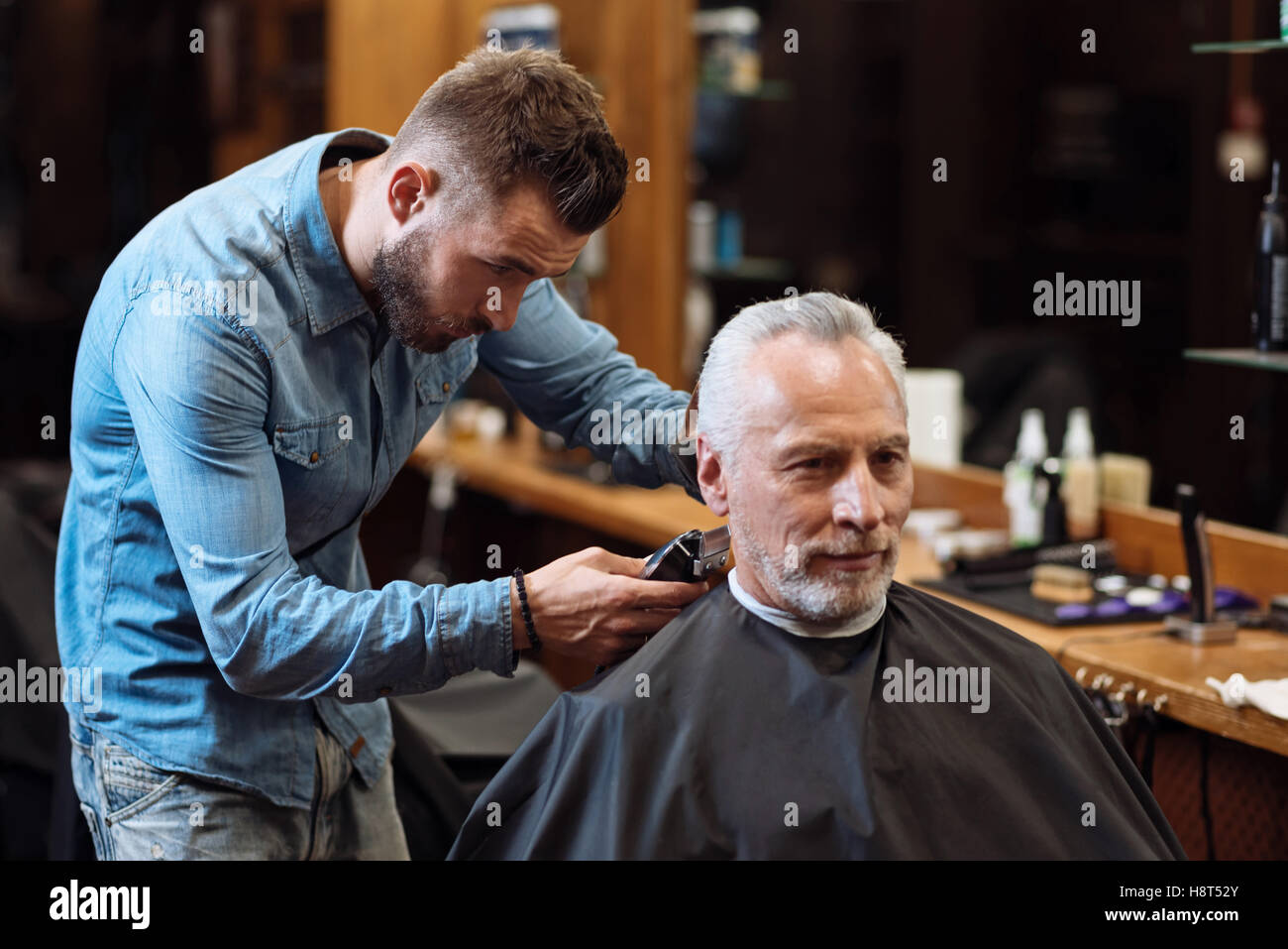 Handsome barber trimming hair of old man Stock Photo - Alamy