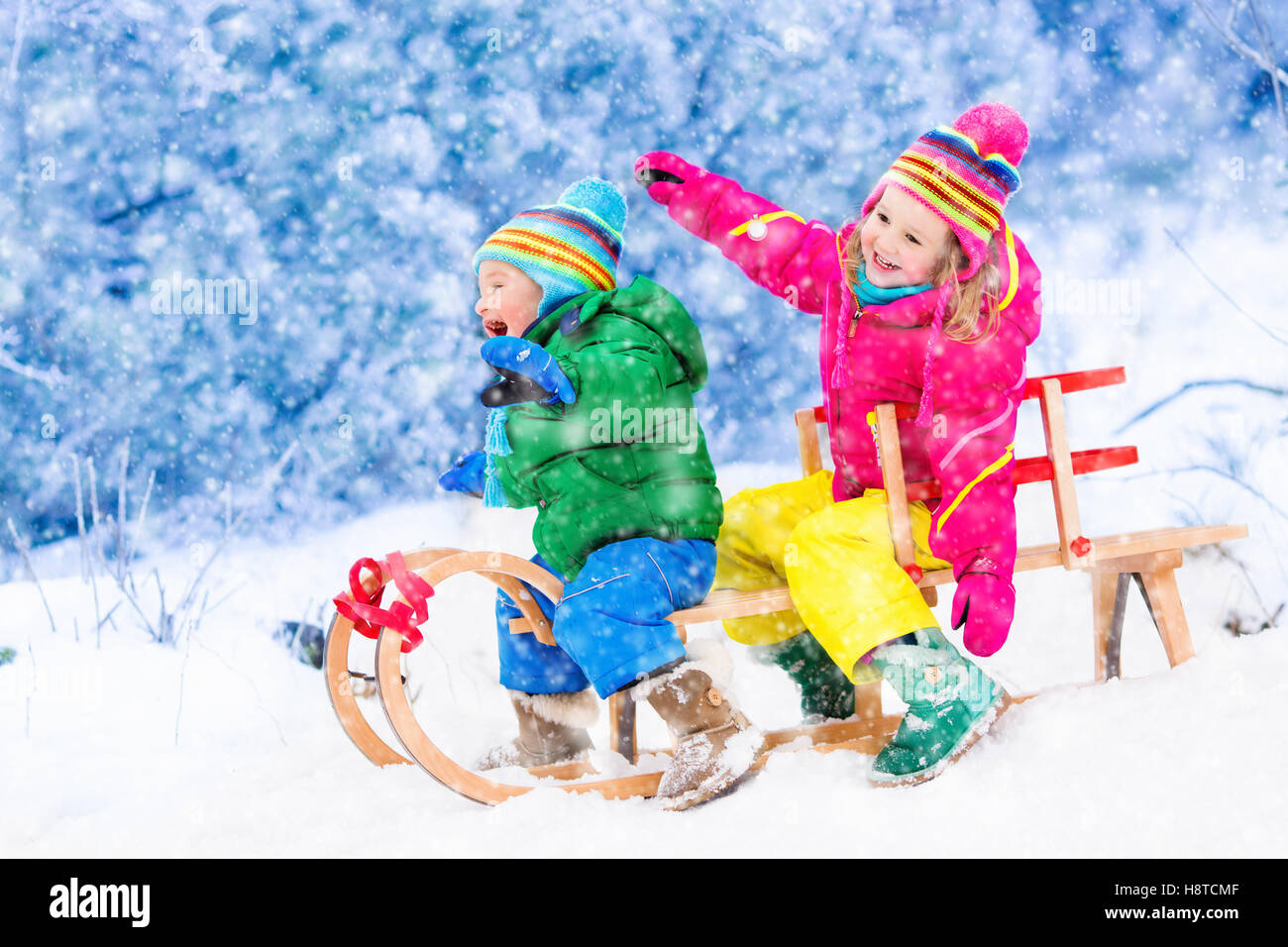 Little girl and boy enjoying sleigh ride. Child sledding. Toddler kid riding a sledge. Children ...