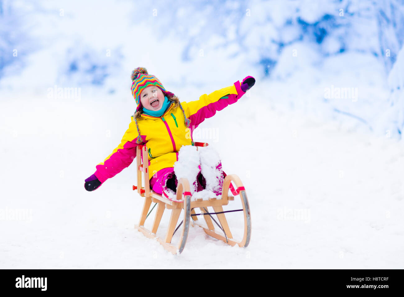 Little girl enjoying sleigh ride. Child sledding. Toddler kid riding a sledge. Children play ...