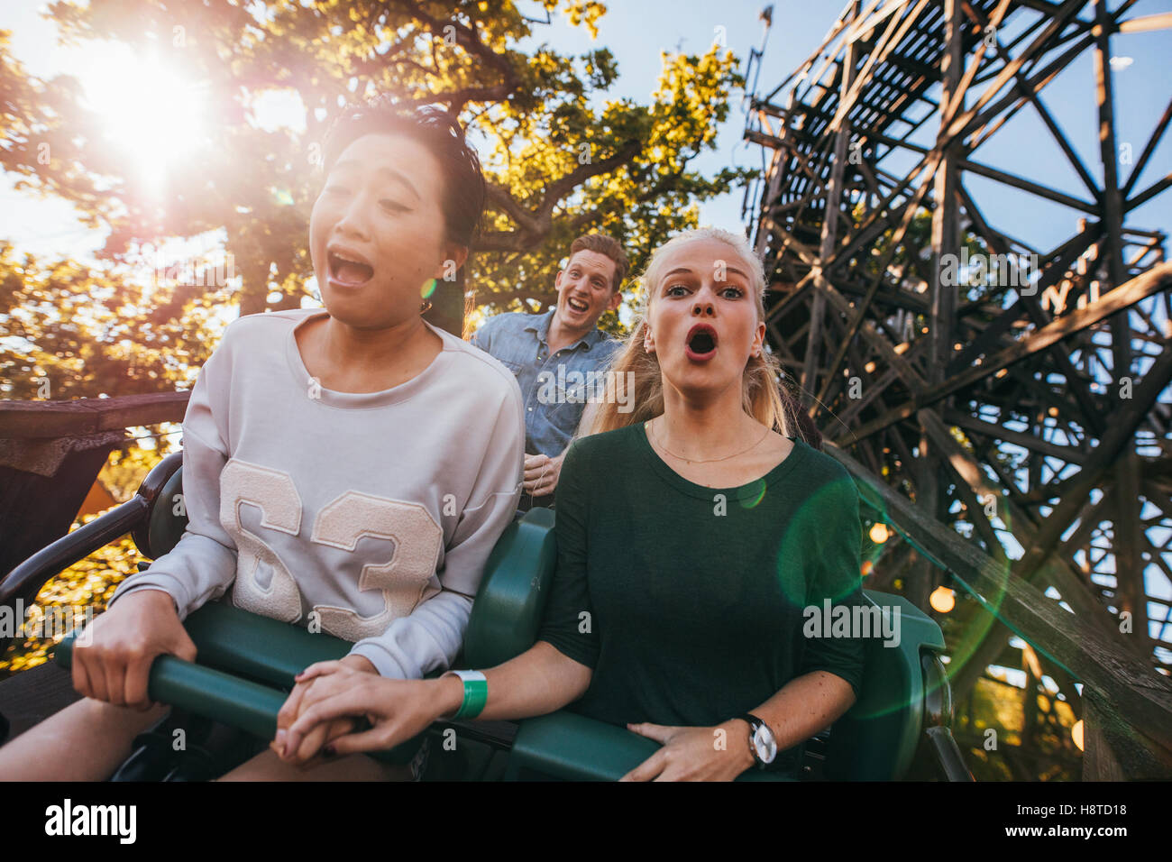 Shot of young friends enjoying riding roller coaster at amusement park ...