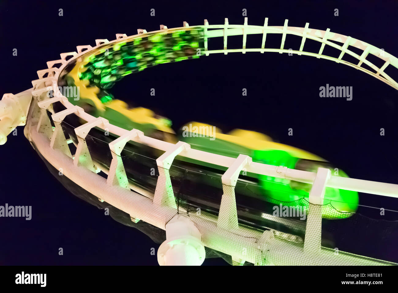 High-speed neon green roller coaster looping at night with motion blur ...