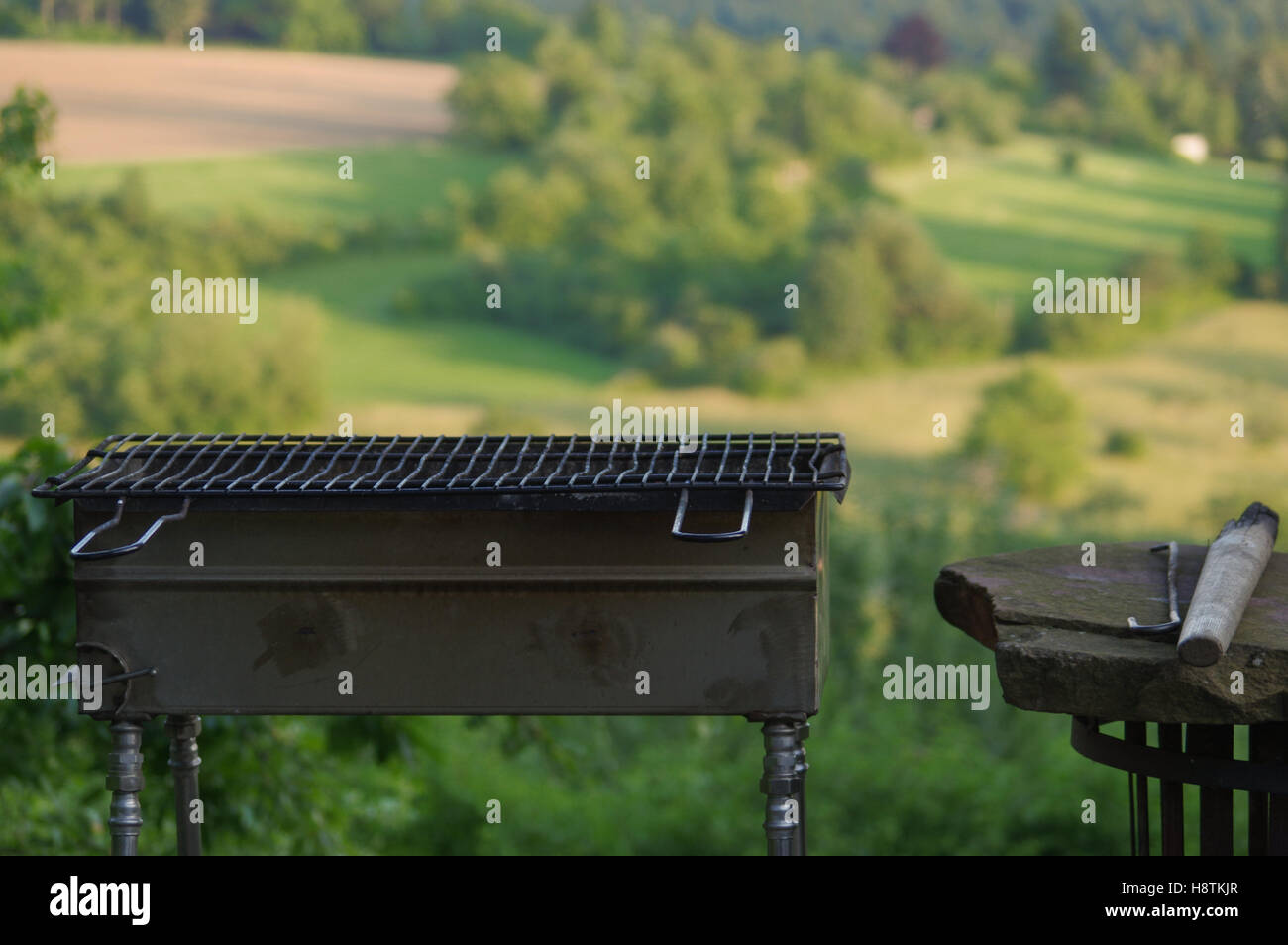 a empty portable BBQ grill in front of a fresh green summer landscape ...