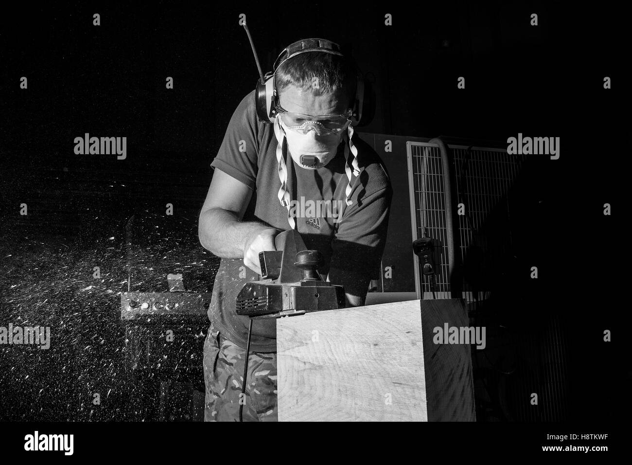 Furniture maker wearing personal protection equipment planing a piece ...