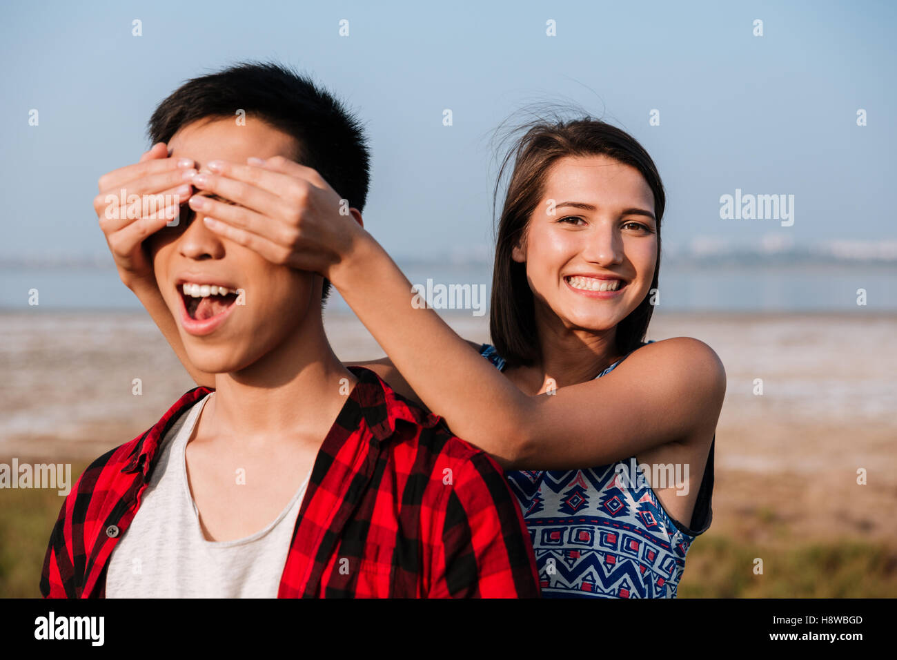 Happy cute young woman covered eyes by hands to her boyfriend outdoors ...