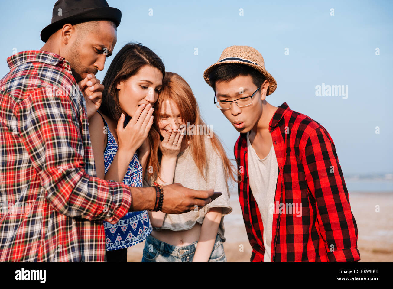 Group of amazed young people standing and looking at screen of cell ...