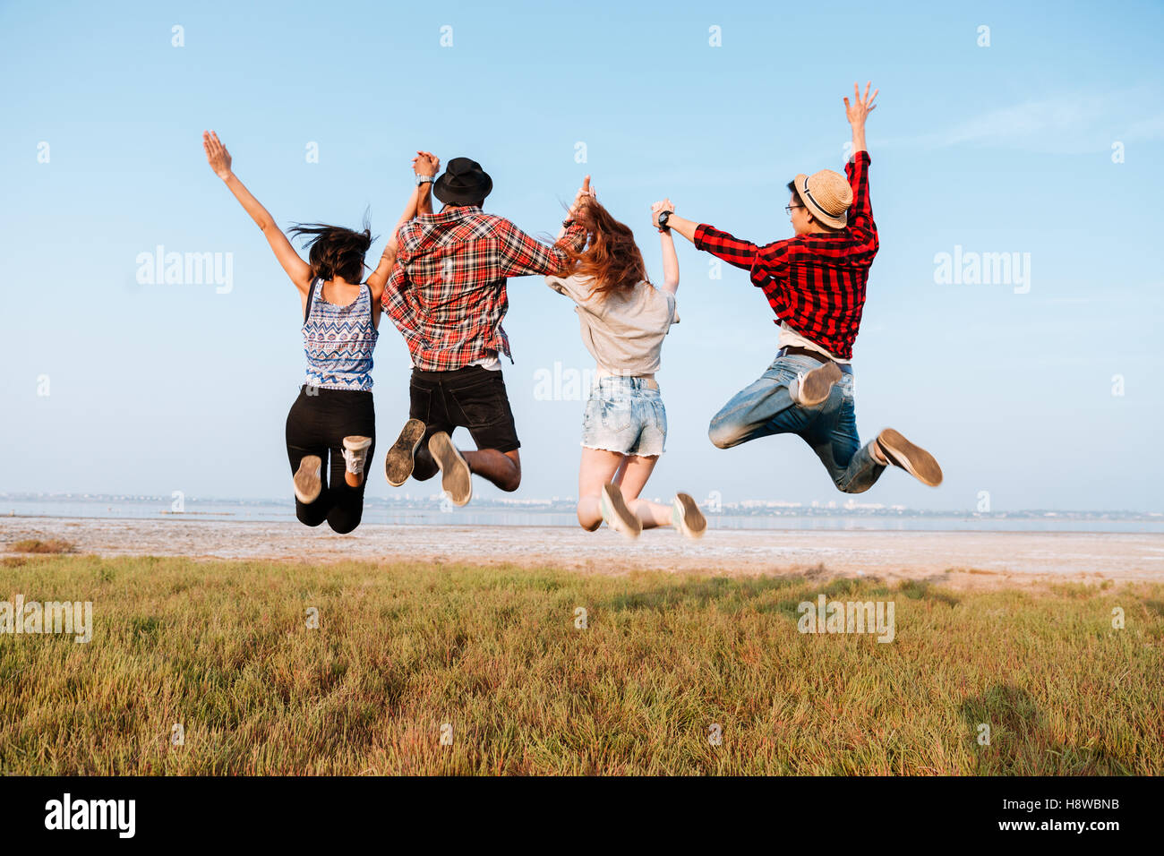 Back view of happy excited young people holding hands and jumping in ...