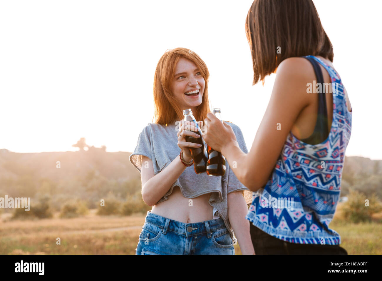 Two smiling young women standing and drinking soda outdoors Stock Photo ...