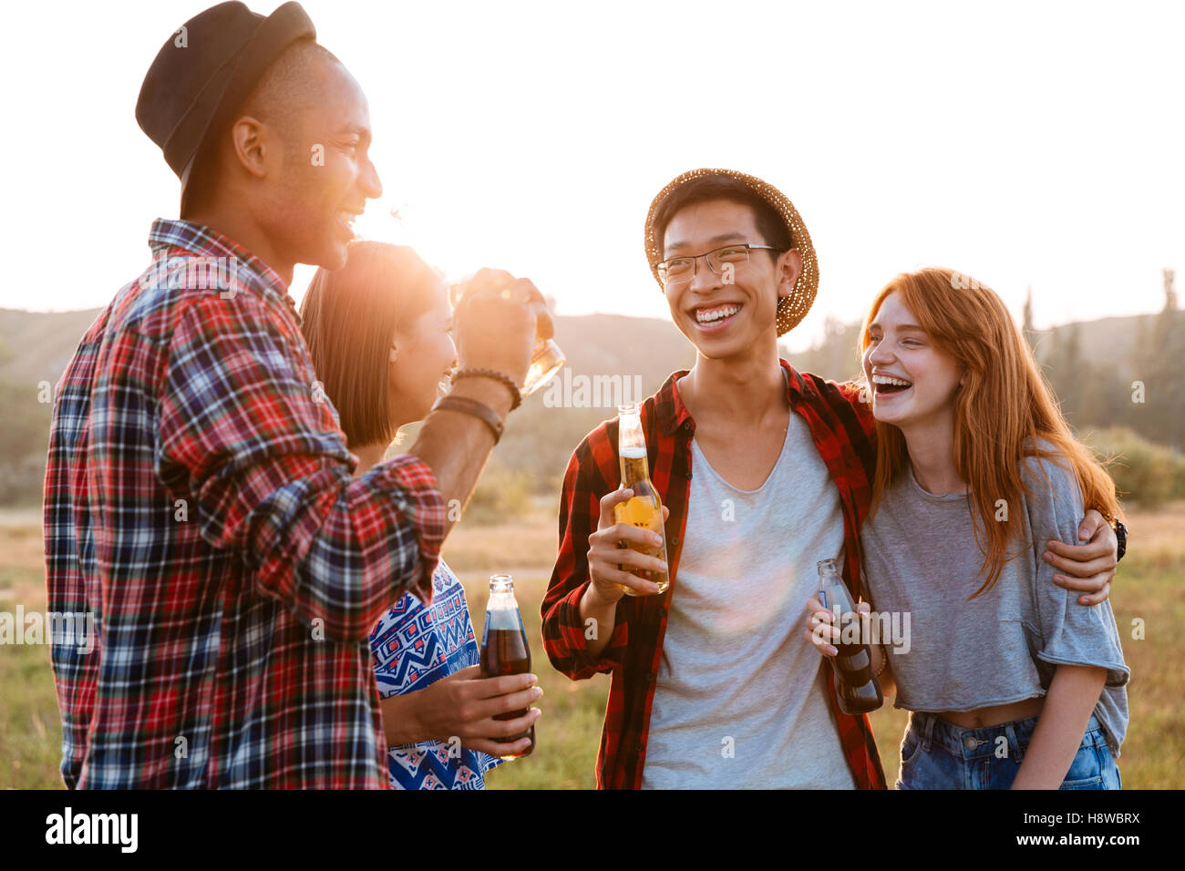 Two happy young couples talking and drinking beer and soda together ...