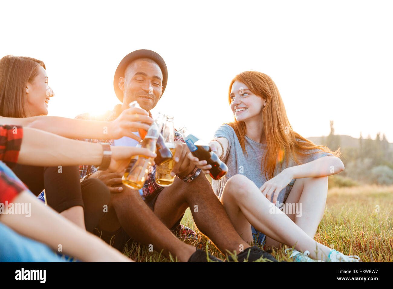 Group of happy young friends sitting and drinking beer and soda ...