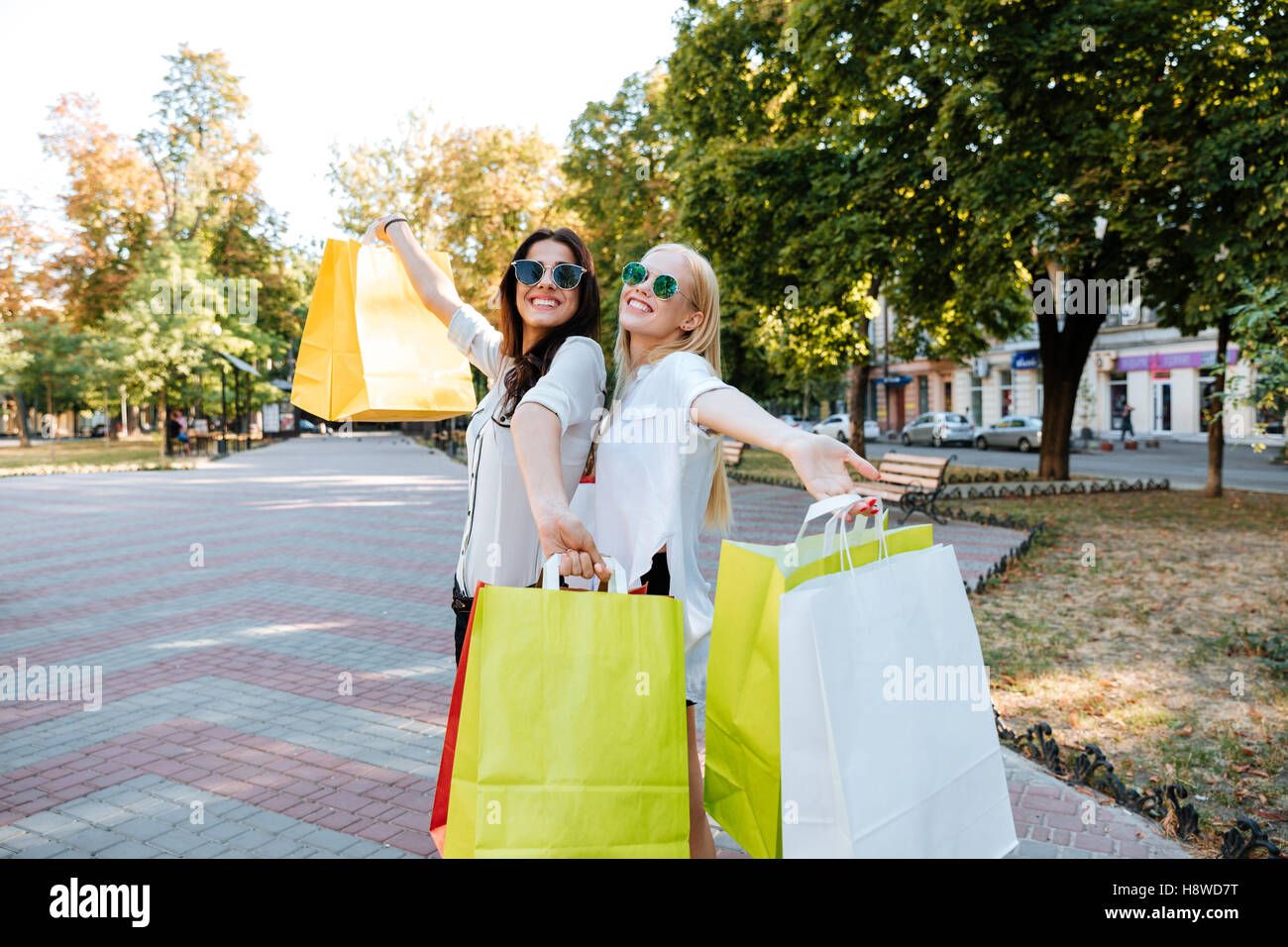 Two women shoppers in sunglasses holding shopping bags and walking in ...