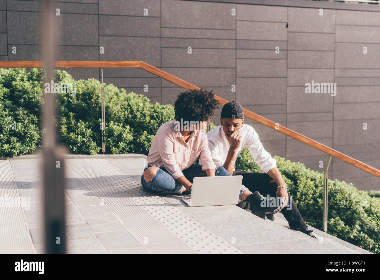Young multiethnic couple using computer sitting outdoor in the city ...